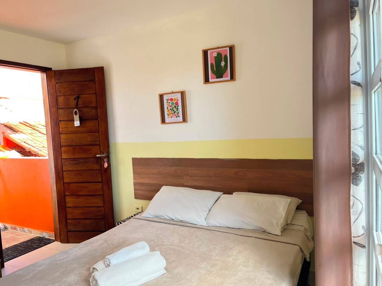 Quarto de hotel com uma cama, uma porta de madeira e duas molduras na parede.