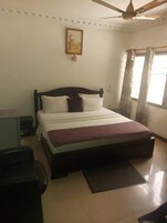 Quarto com cama, ventoinha no teto, quadro e janela com cortinas.