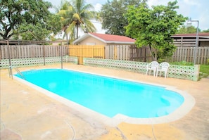 Uma piscina retangular com revestimento de azulejos, rodeada por uma cerca de madeira e uma vedação de madeira verde.