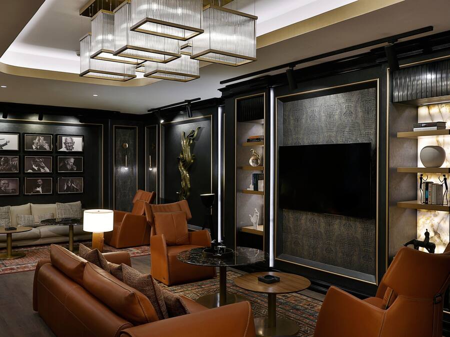 Uma sala de estar moderna com sofás de couro, uma mesa de centro e uma televisão de tela plana grande. Há quadros nas paredes e uma escultura decorativa.