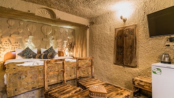 Quarto com cama, cadeiras de madeira, mesa, televisão e frigorífico.