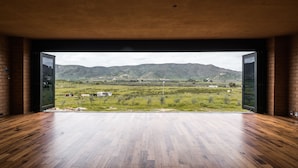 Um quarto espaçoso com piso de madeira e uma grande porta de vidro que dá para uma vista panorâmica de montanhas e campos.