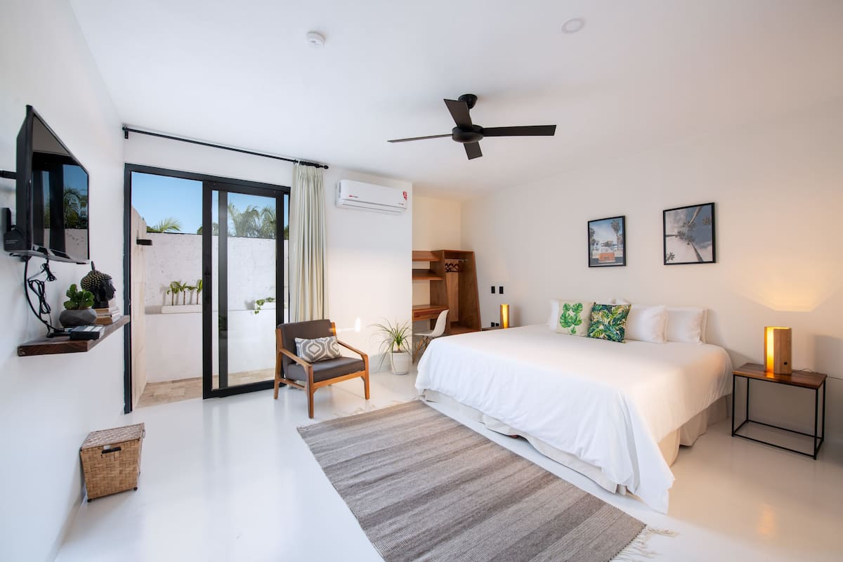 Quarto moderno com uma cama grande, ventoinha no teto, escrivaninha e porta de vidro corria para uma varanda.