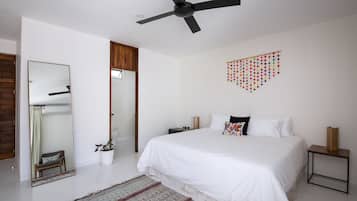 Um quarto moderno com uma cama grande, um ventilador de teto, um espelho, uma decoração pendente e uma mesinha de cabeceira.