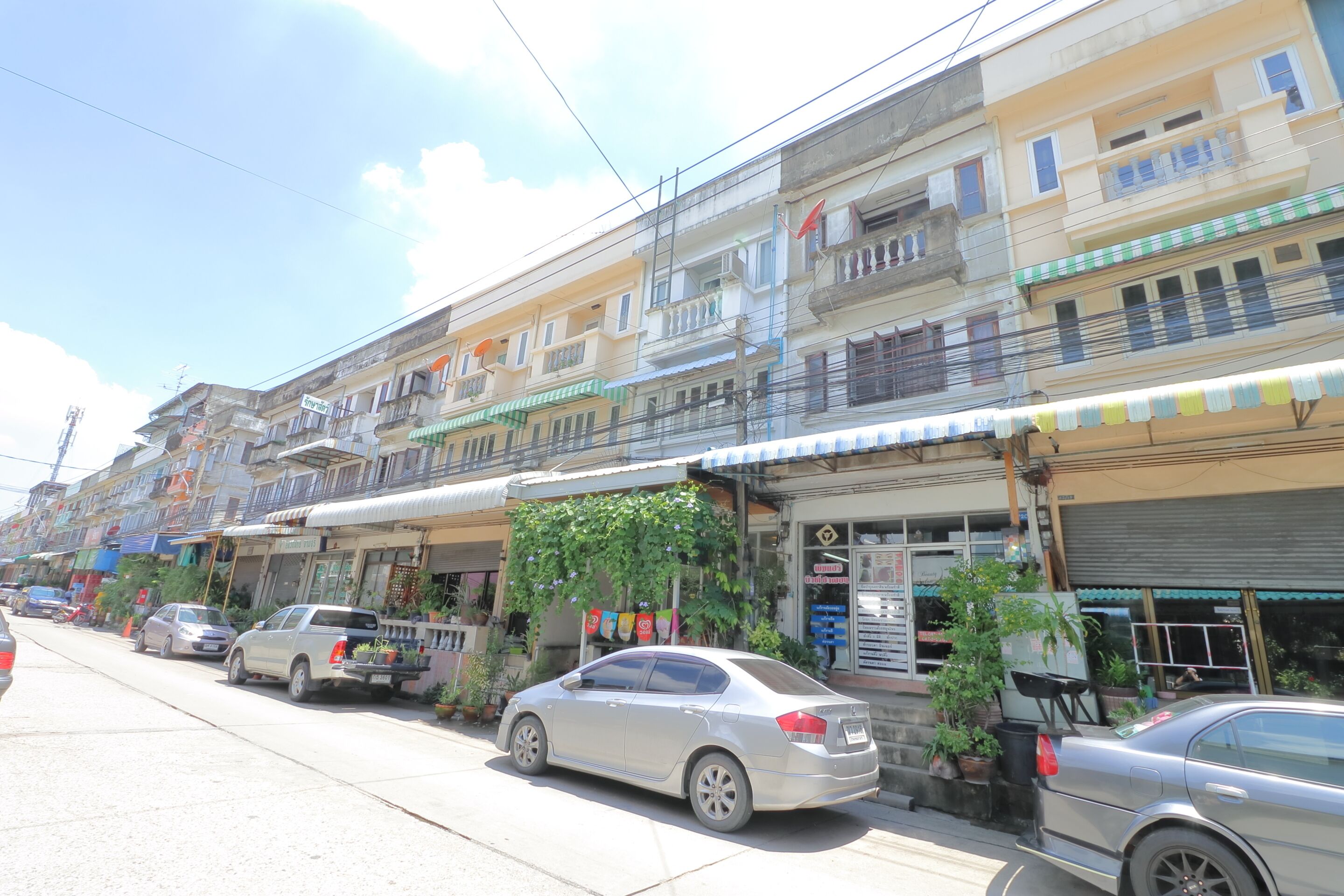 Vista da rua com edifícios altos, carros estacionados e vitrines visíveis.