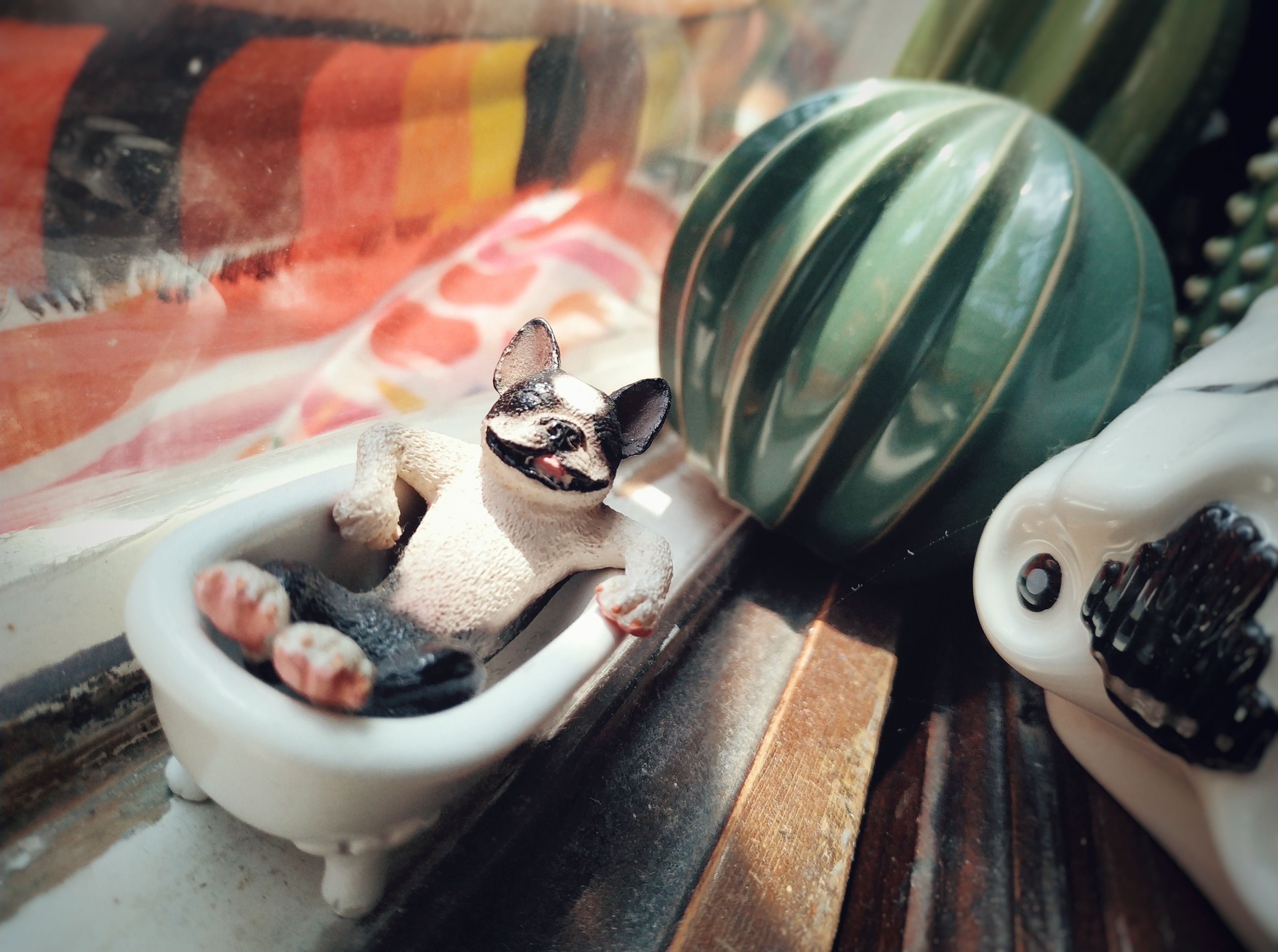 Uma pequena estatueta de cachorro em um vaso sanitário branco, um vaso verde listrado e um objeto de cerâmica branca com detalhes pretos.