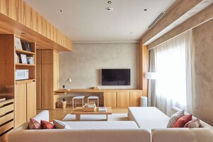 Uma sala de estar moderna com sofá, mesa de centro, televisão de tela plana, armários de madeira e uma janela grande com cortinas.