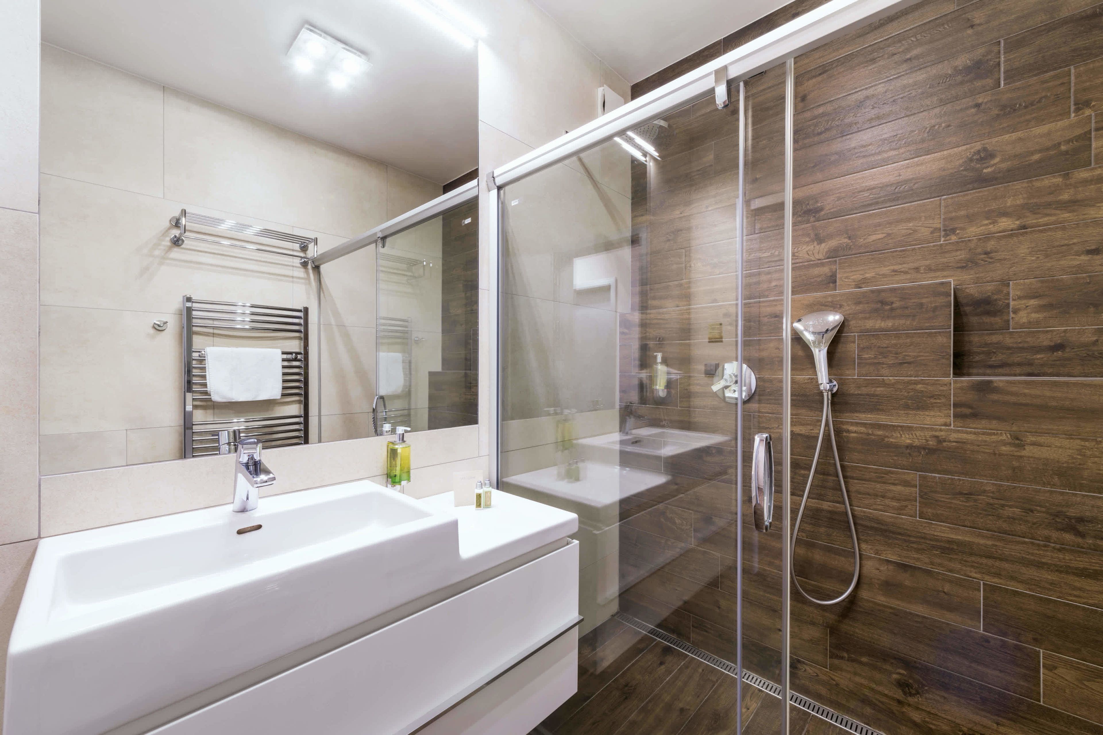 Casa de banho moderna com chuveiro envidraçado, espelho grande e toucador branco com duas pias.