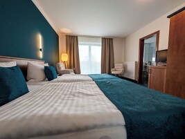 Quarto de hotel com cama, duas poltronas, uma escrivaninha, abajur e vista para o exterior.