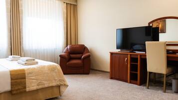 Quarto de hotel com cama, uma poltrona de couro marrom, escrivaninha com televisão e armário de madeira.