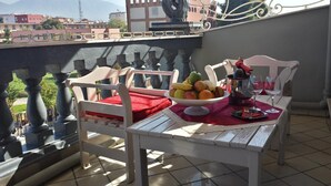 Varanda com mesa branca posta para dois, com fruteira, taça de vinho e uma estátua decorativa.