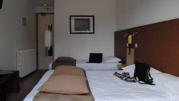 Quarto de hotel com duas camas, uma escrivaninha, uma cadeira, um radiador, uma citação emoldurada na parede e um telefone.