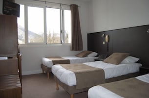 Quarto de hotel com duas camas, uma cômoda de madeira, uma escrivaninha, um telefone e uma janela com cortinas.