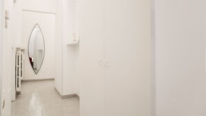 Um corredor com uma porta branca, um radiador e um espelho na parede.
