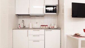 Cozinha moderna com armários brancos, forno de aço inoxidável e televisão de tela plana na parede.