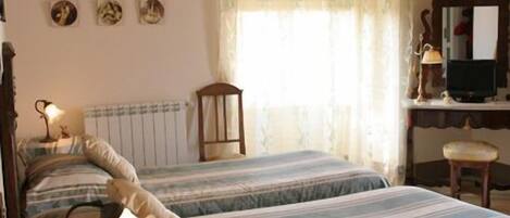 Quarto com duas camas, teto de madeira, escrivaninha com cadeira e janela com cortina.