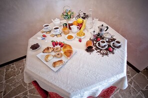 Mesa de pequeno-almoço com pastelaria, frutas, café e uma bicicleta.