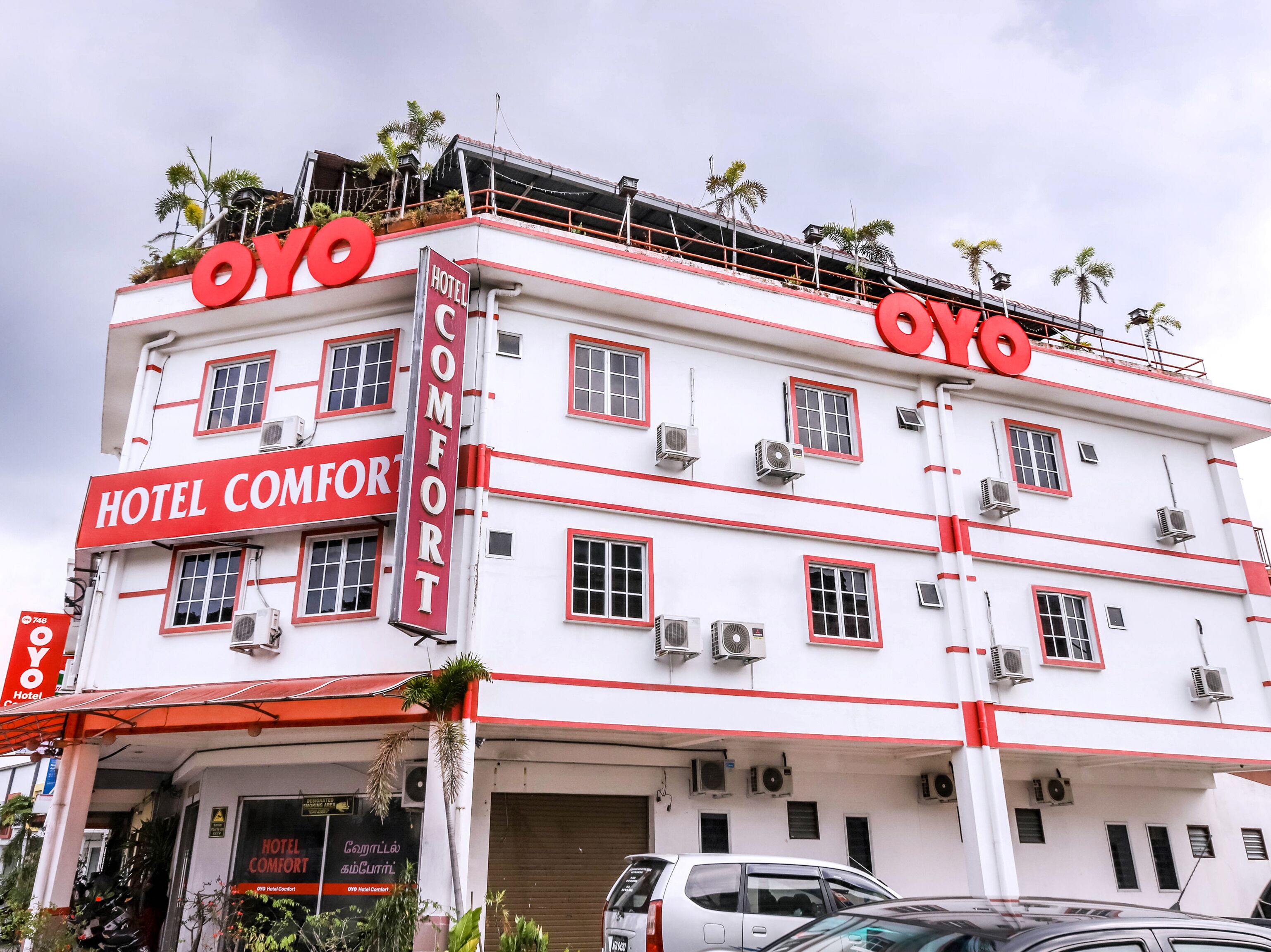 Um edifício de hotel com vários andares, com a sinalização "OYO Hotel Comfort", unidades de ar condicionado e um toldo vermelho.