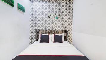Uma cama com colcha branca e vermelha, duas almofadas pretas e uma parede com padrão e texto em árabe.