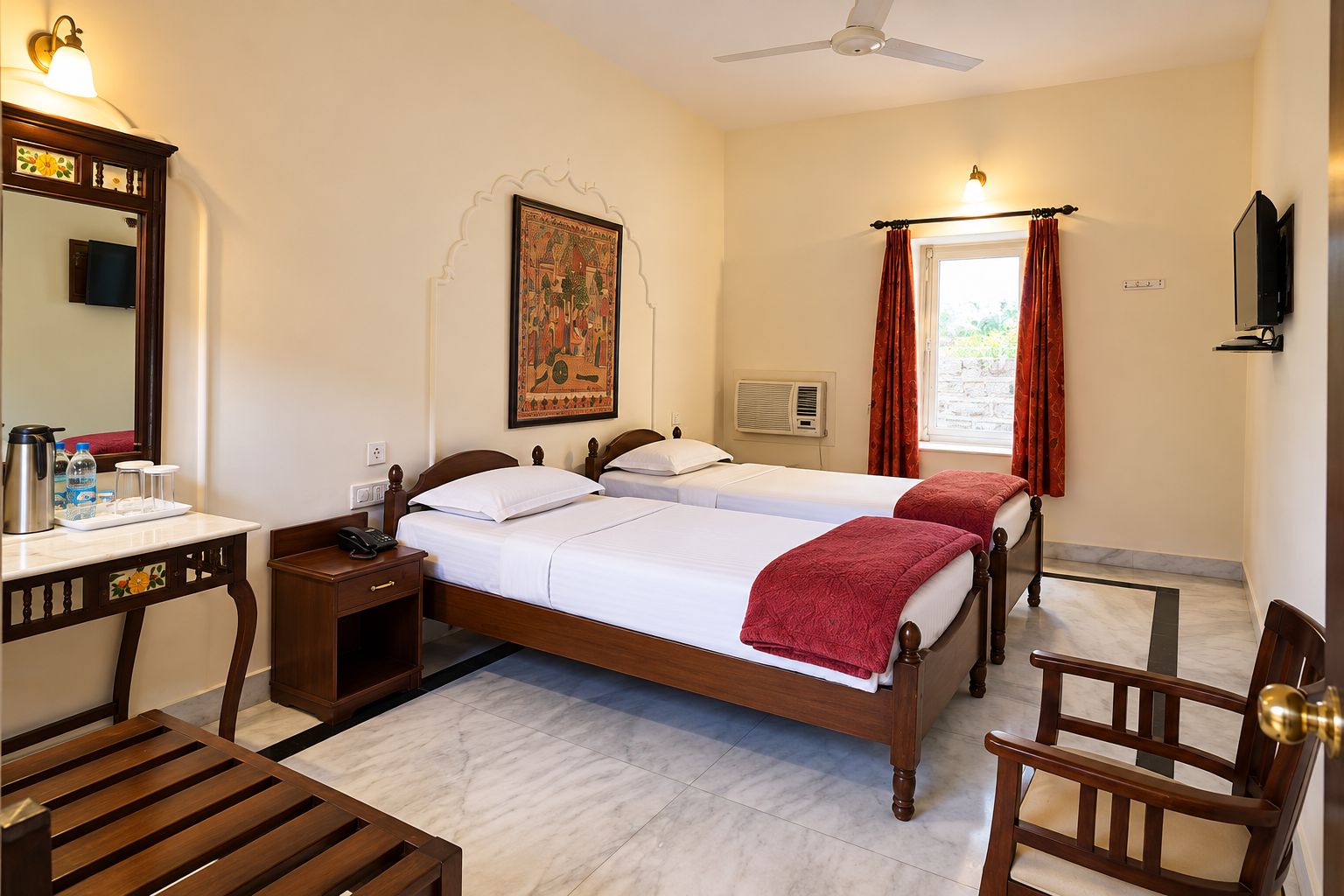 Quarto de hotel com duas camas, uma escrivaninha com telefone, uma cadeira, mesa de cabeceira, televisão na parede e ventoinha no teto.