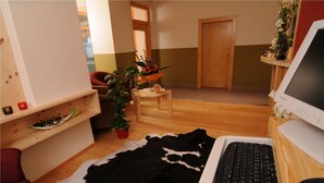 Quarto com escrivaninha de madeira, computador, teclado, rato, tapete de couro bovino, cadeira vermelha, prateleira de madeira com objetos decorativos e planta em vaso.
