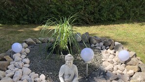 Uma estátua de Buda rodeada por pedras e plantas, com três luzes esféricas.