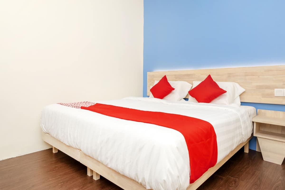 Uma cama bem arrumada com roupa de cama branca e vermelha, uma cabeceira de madeira e uma mesa de cabeceira com um abajur.