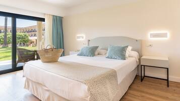 Quarto de hotel com uma cama grande, mesa de cabeceira, abajur, janela com cortinas e vista para o edifício.