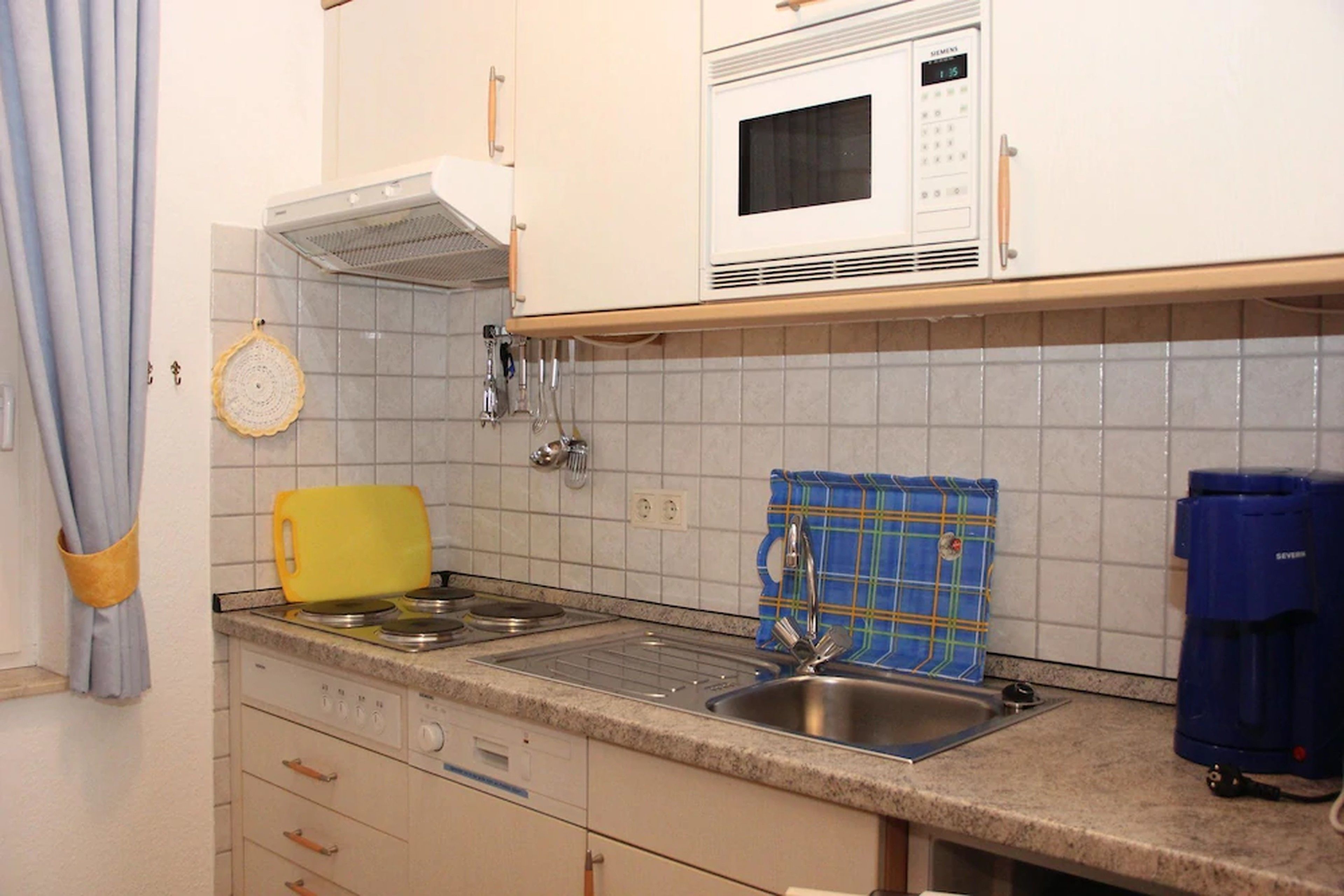 Uma cozinha com micro-ondas, fogão, pia e uma toalha azul pendurada na parede.