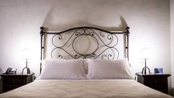 Uma cama bem arrumada com cabeceira de metal, duas mesas de cabeceira com luminárias e um telefone em uma delas.