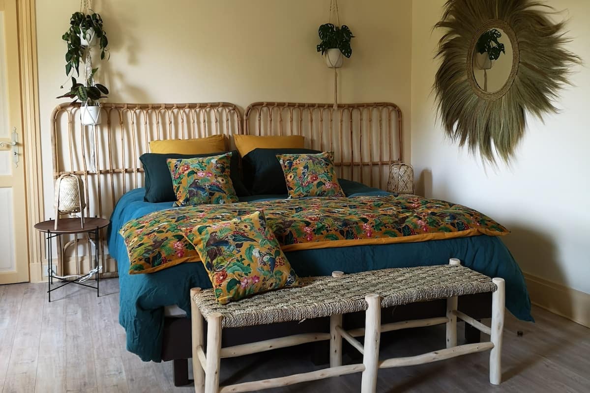 Quarto com cama, um banquinho, luminária pendente e um ornamento na parede.