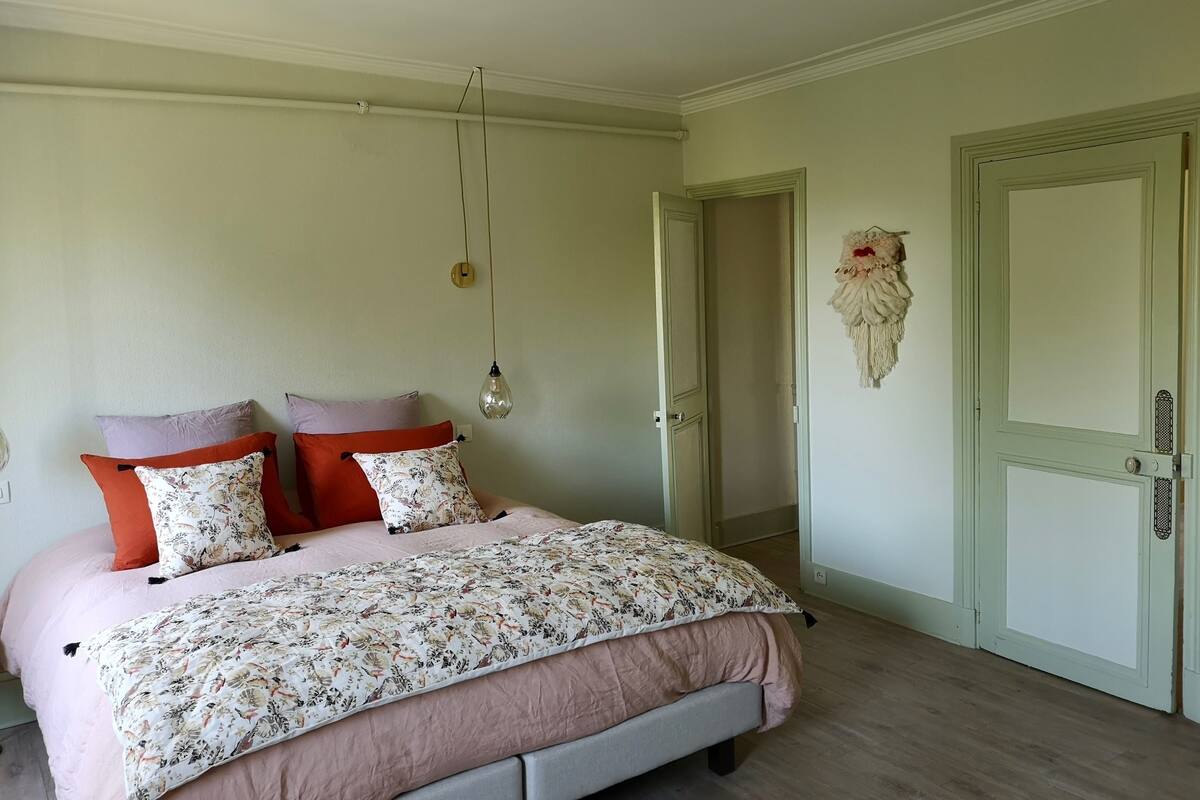 Quarto com cama, almofadas, luminária pendente e porta.