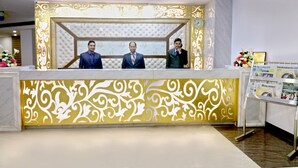 Uma mesa de recepção com três homens em pé atrás dela, um relógio e um arranjo de flores.