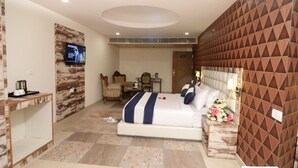 Quarto de hotel com cama, televisão fixada na parede, escrivaninha com cadeira e painel decorativo.