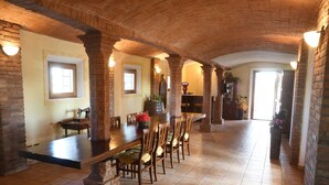 Uma sala de jantar espaçosa com uma mesa comprida, diversas cadeiras e arcos de tijolo.