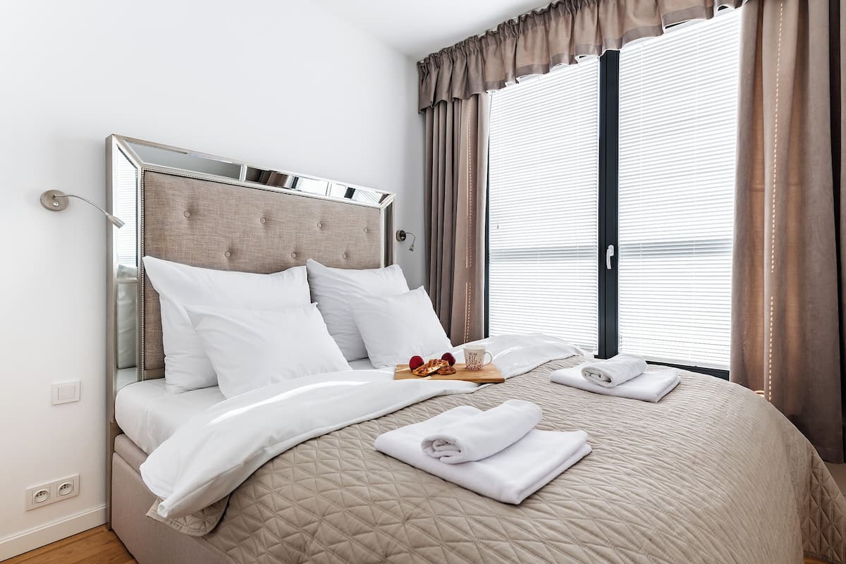 Uma cama bem arrumada com lençóis brancos, uma bandeja com petiscos e uma toalha dobrada sobre a cama.