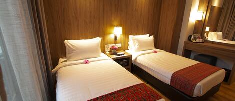 Quarto de hotel com duas camas, painéis de madeira nas paredes, uma escrivaninha com espelho e uma mesa de cabeceira com abajur e uma flor.