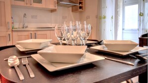 Mesa de jantar posta com pratos, tigelas e talheres brancos, com copos de vinho dispostos ao centro.