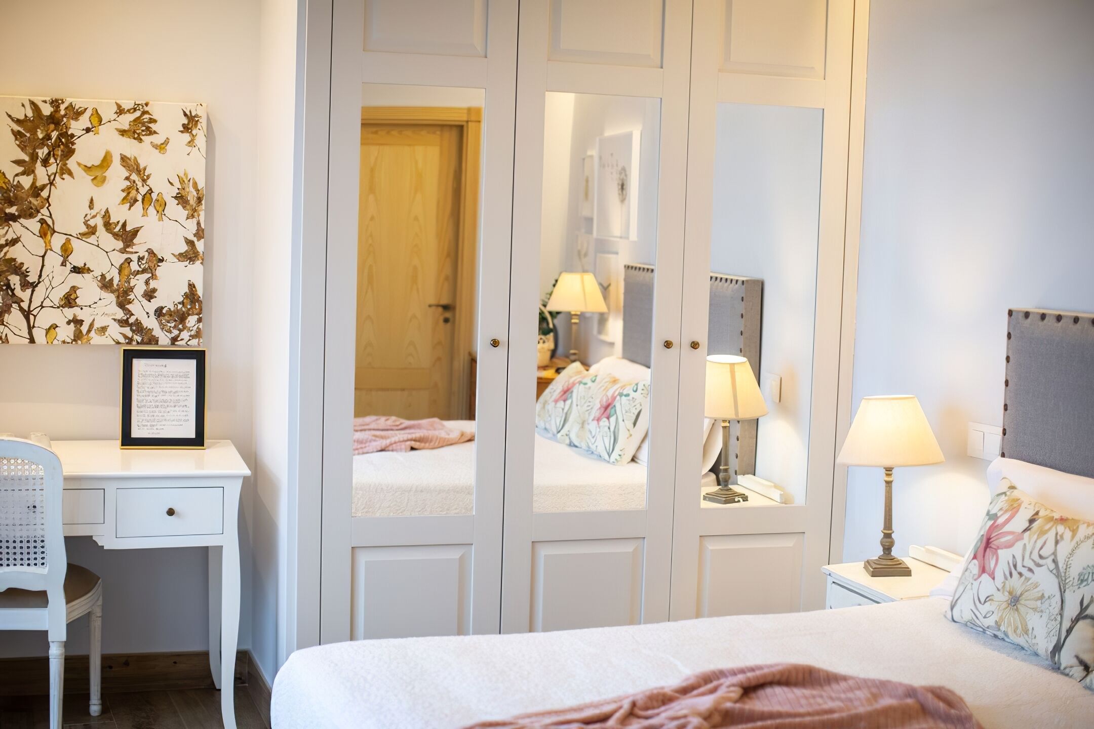 Quarto com cama, mesas de cabeceira, escrivaninha, cadeira e um espelho grande.