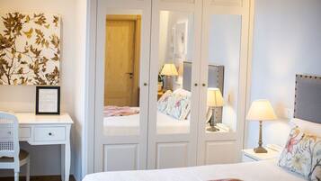 Quarto com cama, mesas de cabeceira, escrivaninha, cadeira e um espelho grande.