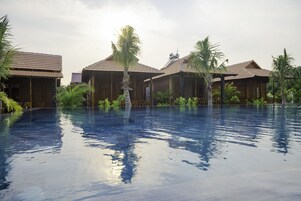 Um resort com piscina, cercado por edifícios de madeira e palmeiras.