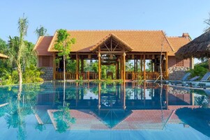Resort com uma piscina grande, estrutura de madeira coberta e vegetação exuberante.