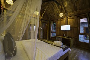Quarto com uma cama, televisão, escrivaninha de madeira e parede de pedra.