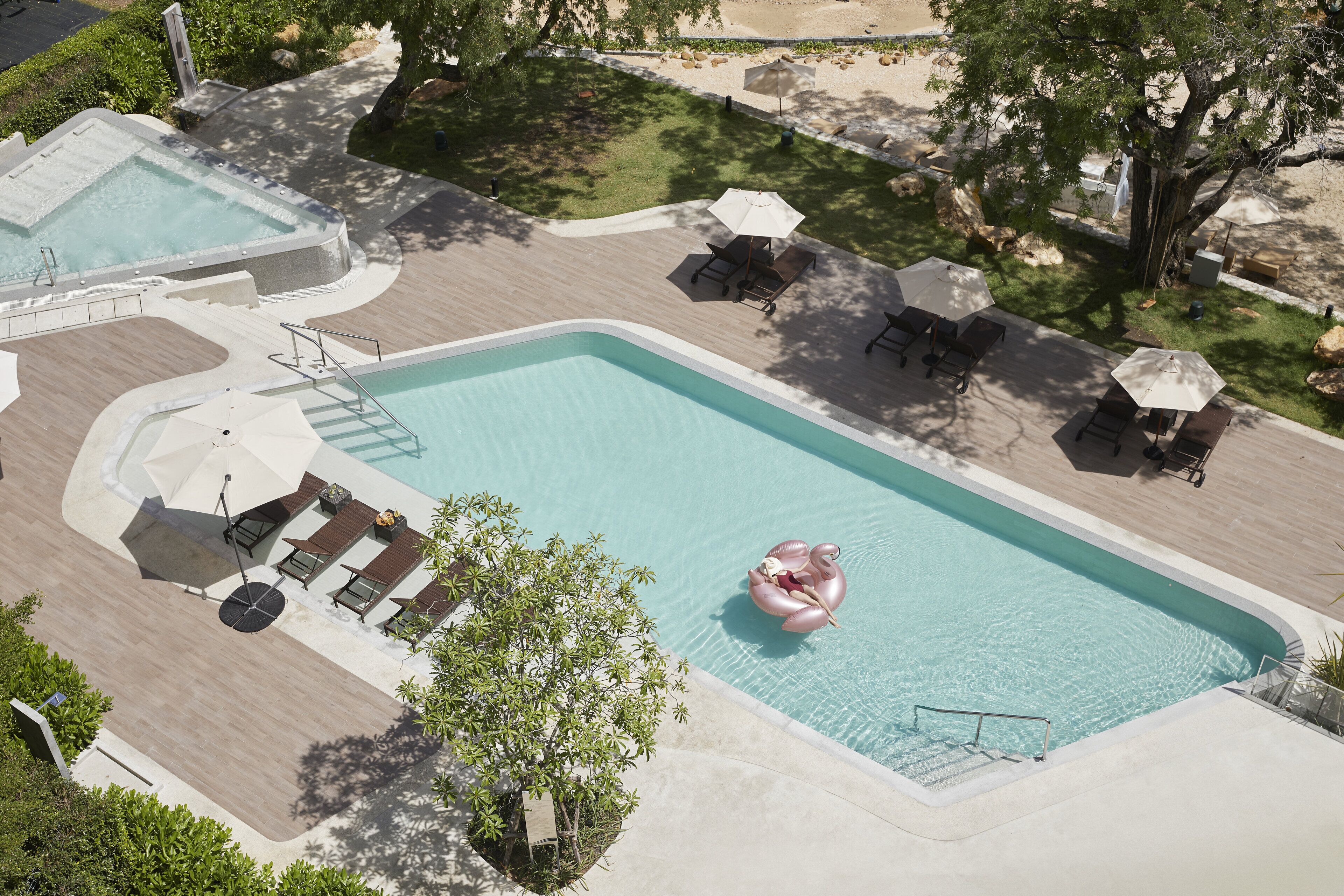 Uma grande piscina retangular com um flutuador de flamingo rosa, cercada por espreguiçadeiras e guarda-sóis.