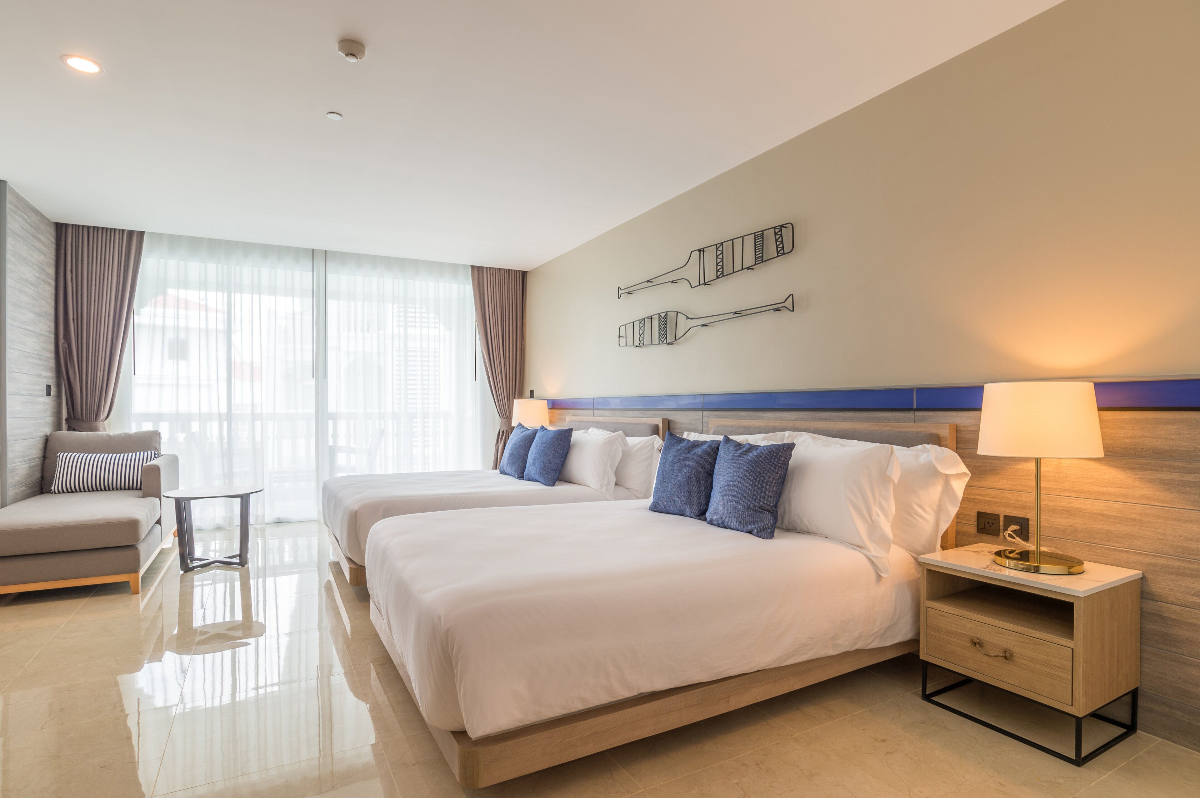 Quarto de hotel com duas camas, um sofá, uma mesa de cabeceira com abajur e uma obra de arte pendurada na parede.