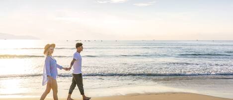 Duas pessoas caminham de mãos dadas na praia.
