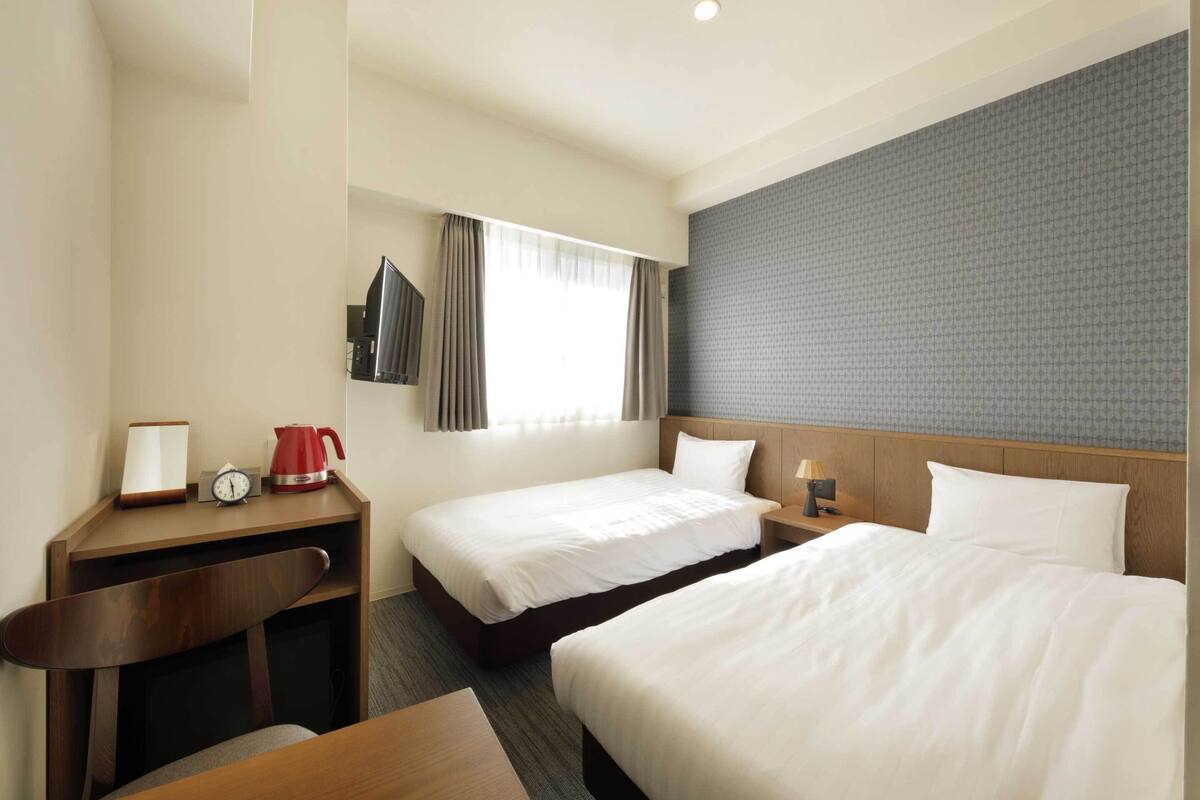 Quarto de hotel com duas camas, uma escrivaninha, uma TV e uma cafeteira.
