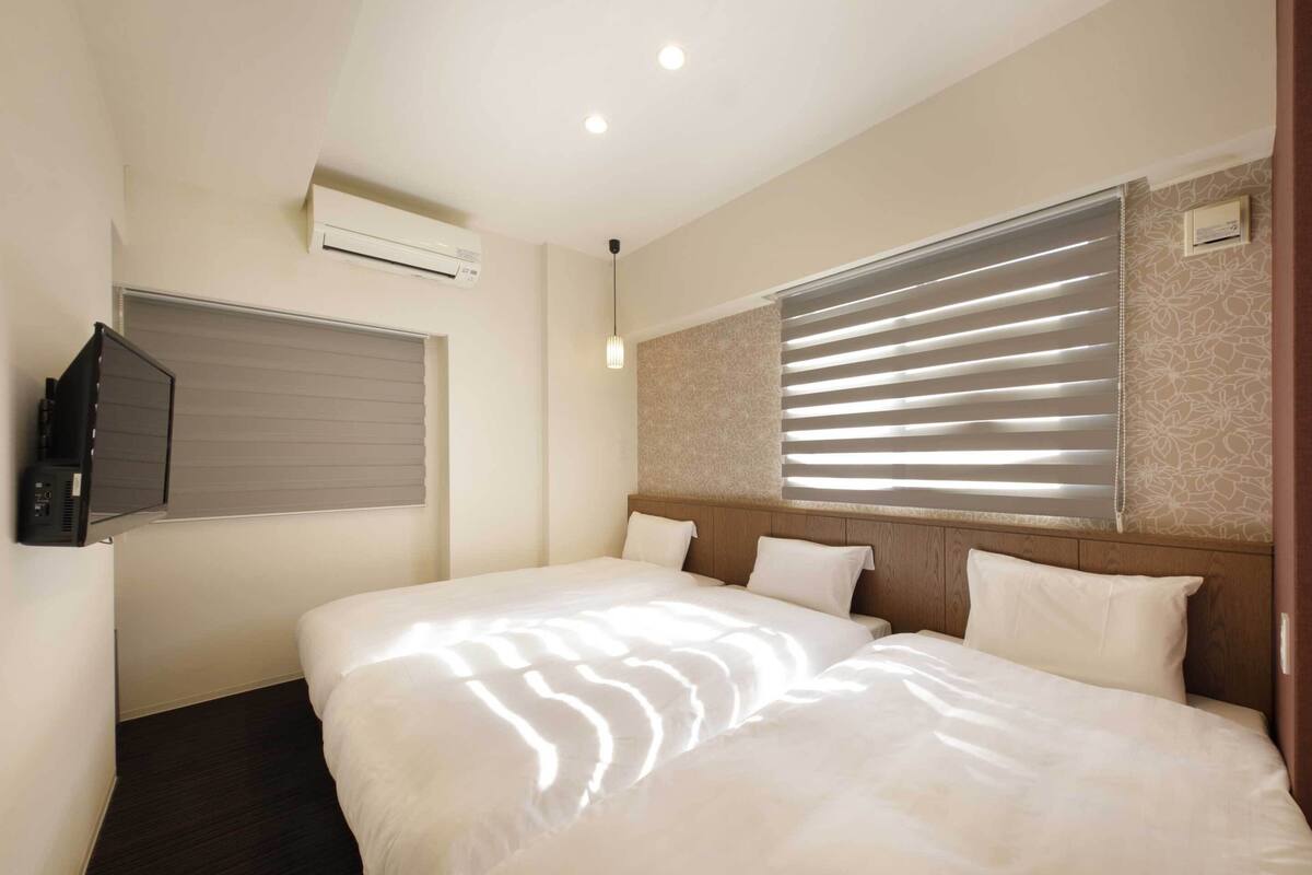 Quarto de hotel com duas camas, televisão de tela plana na parede e ar condicionado.