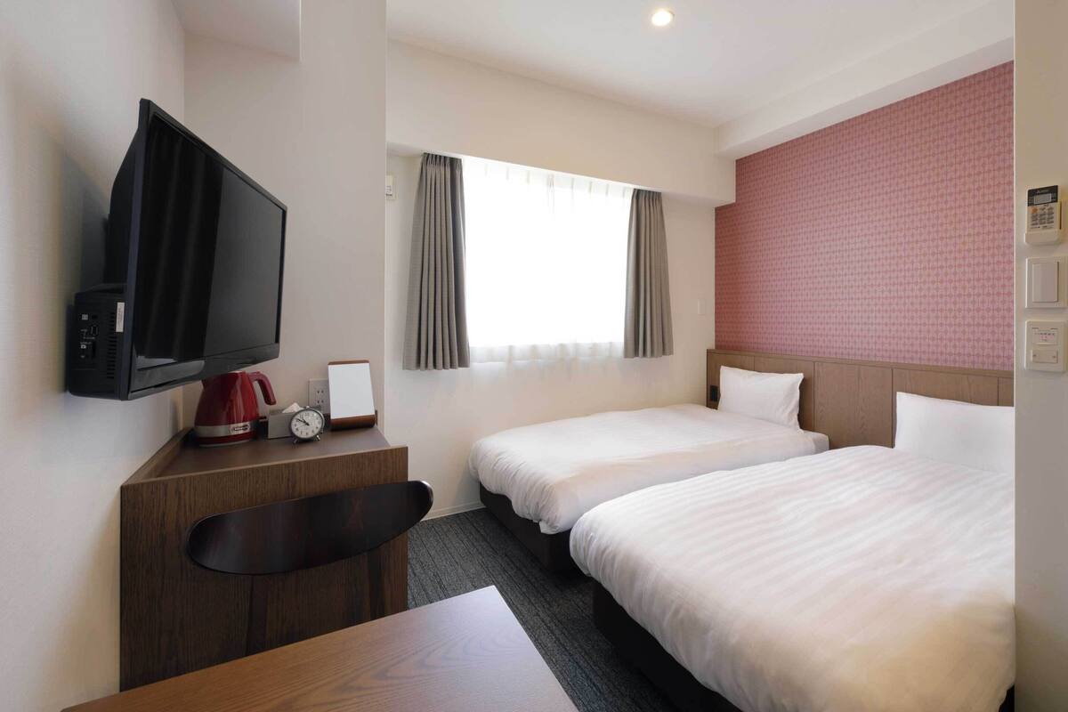Quarto de hotel com duas camas, televisão, máquina de café, relógio e janela com cortinas.