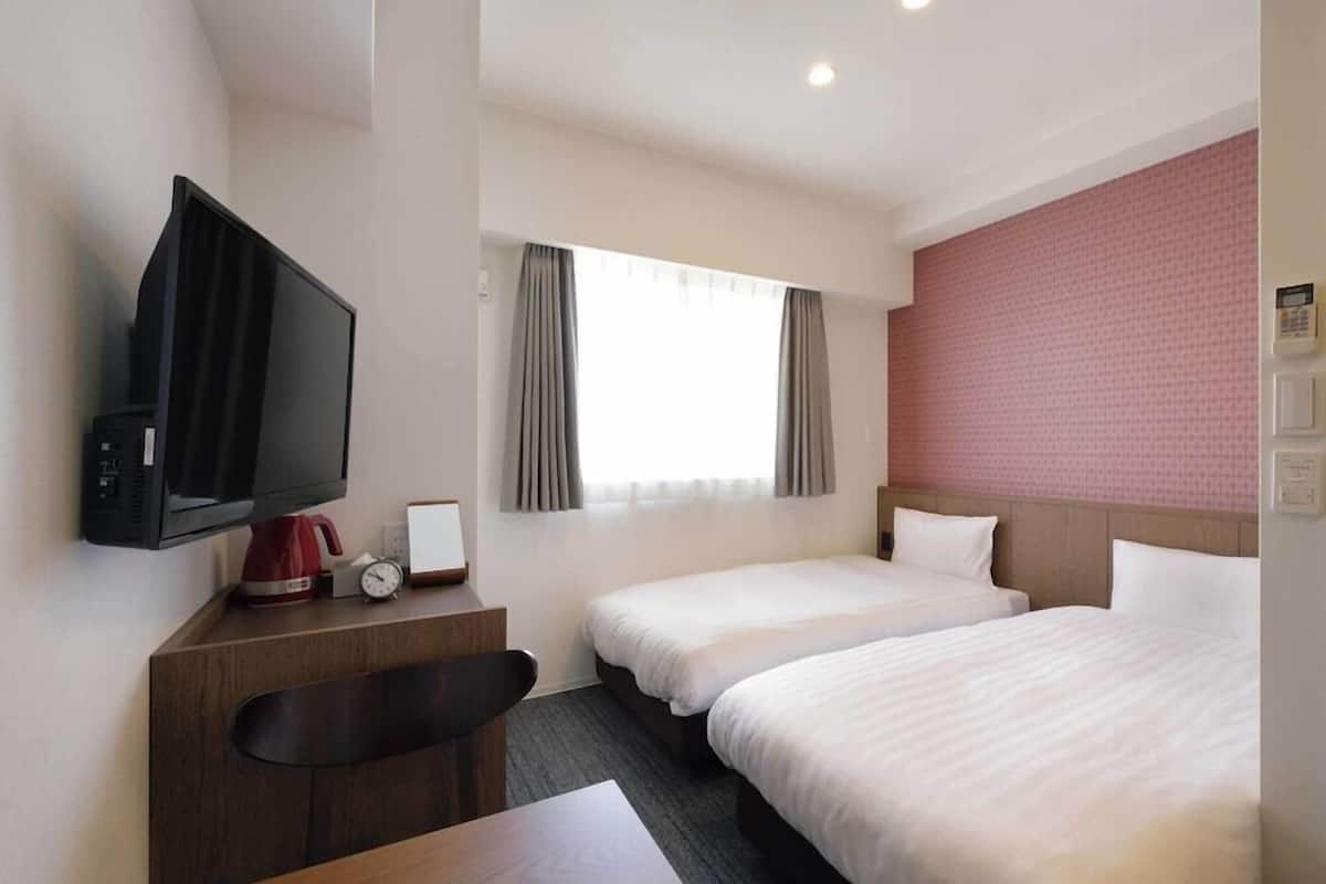 Quarto de hotel com duas camas, televisão, cafeteira, relógio e janela com cortinas.